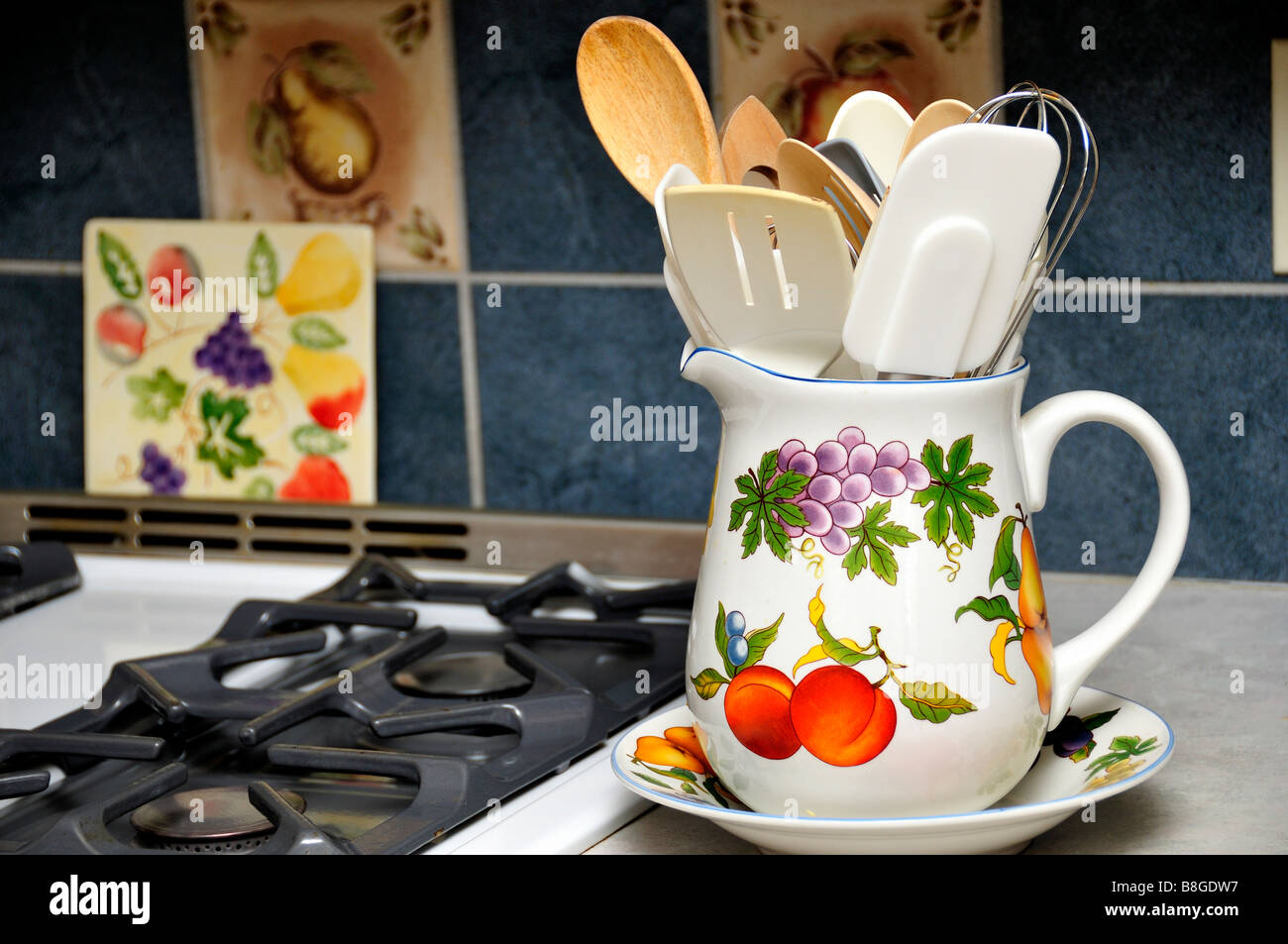 A large, decorated pitcher holding kitchen utensils next to a gas ...