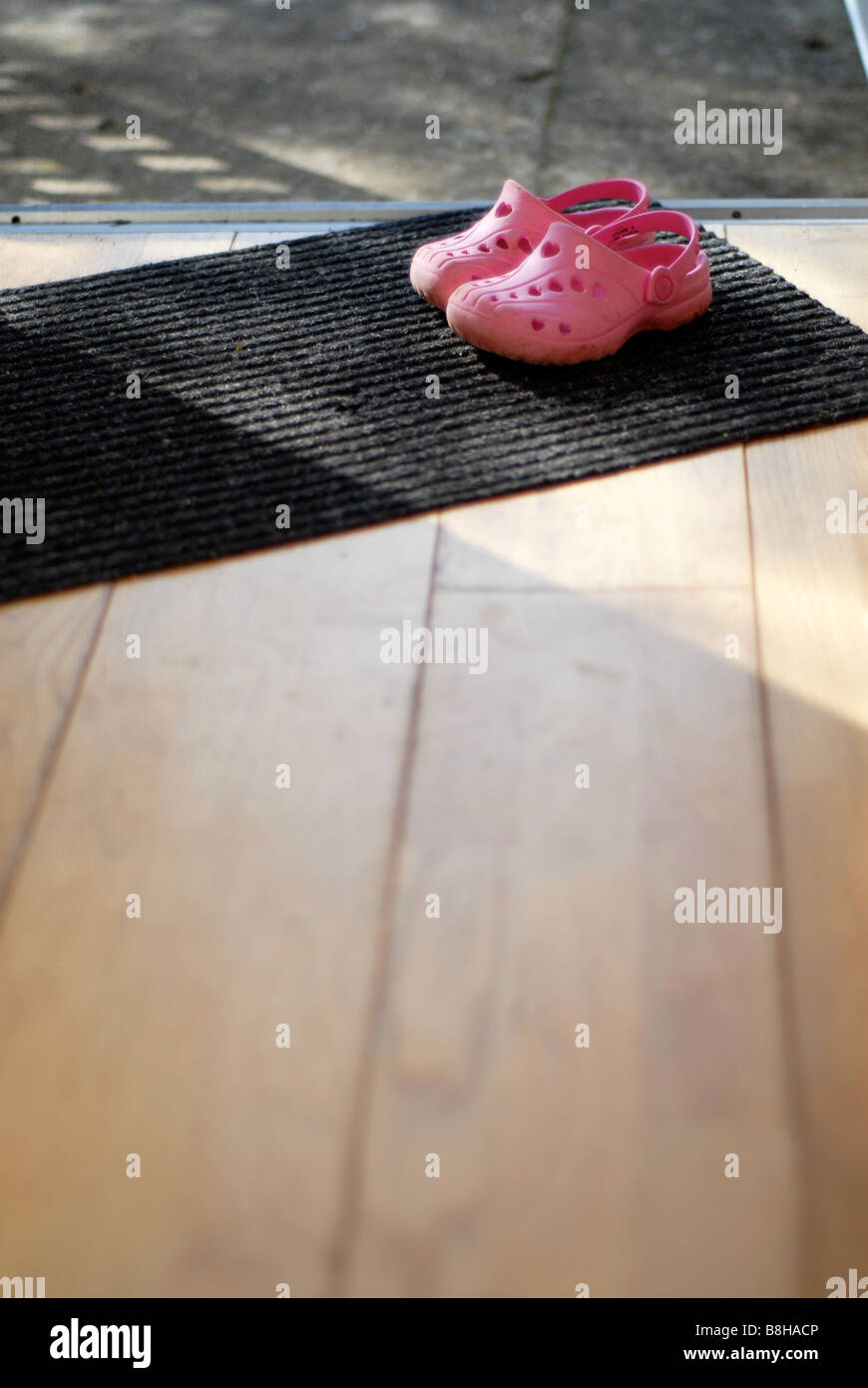 Childs pink croc style outdoor play shoes sitting on the door mat by an ...