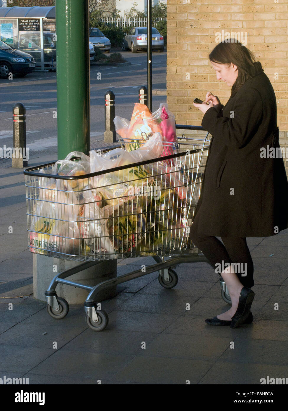UK Woman waiting for taxi with shopping at a supermarket, with trolley ...