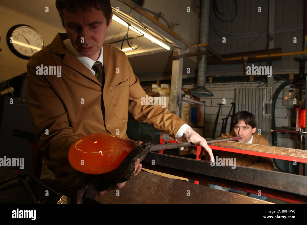 a professional glass blower takes some molten glass out of a furnace ...