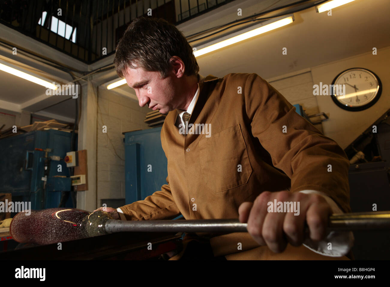 a professional glass blower takes some molten glass out of a furnace ...