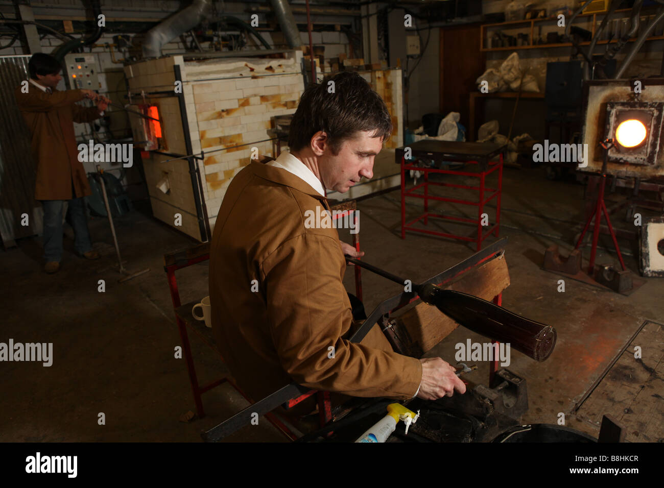 a professional glass blower takes some molten glass out of a furnace ...