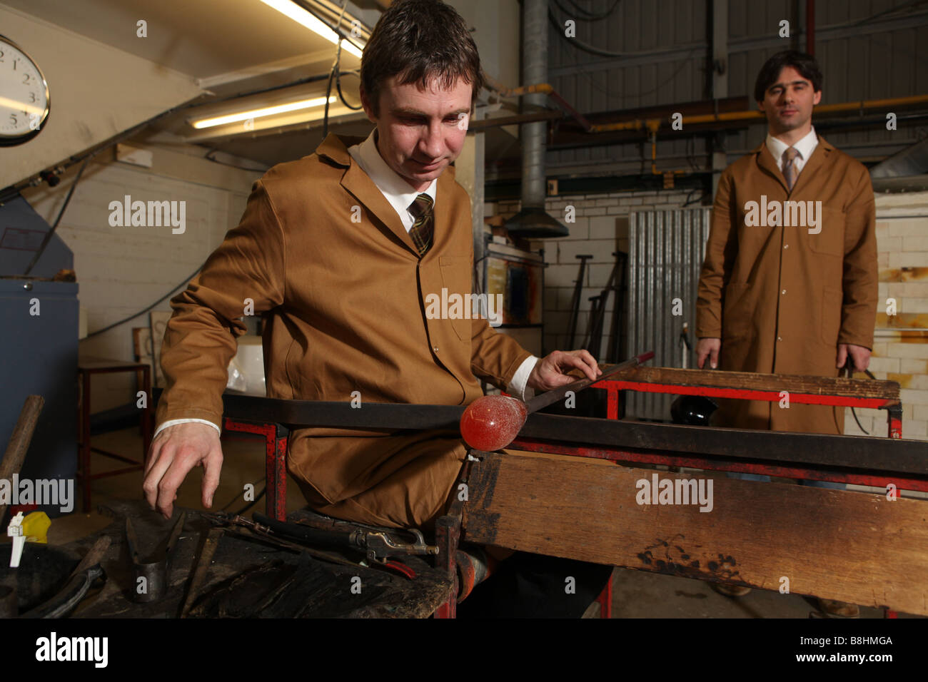 a professional glass blower takes some molten glass out of a furnace ...