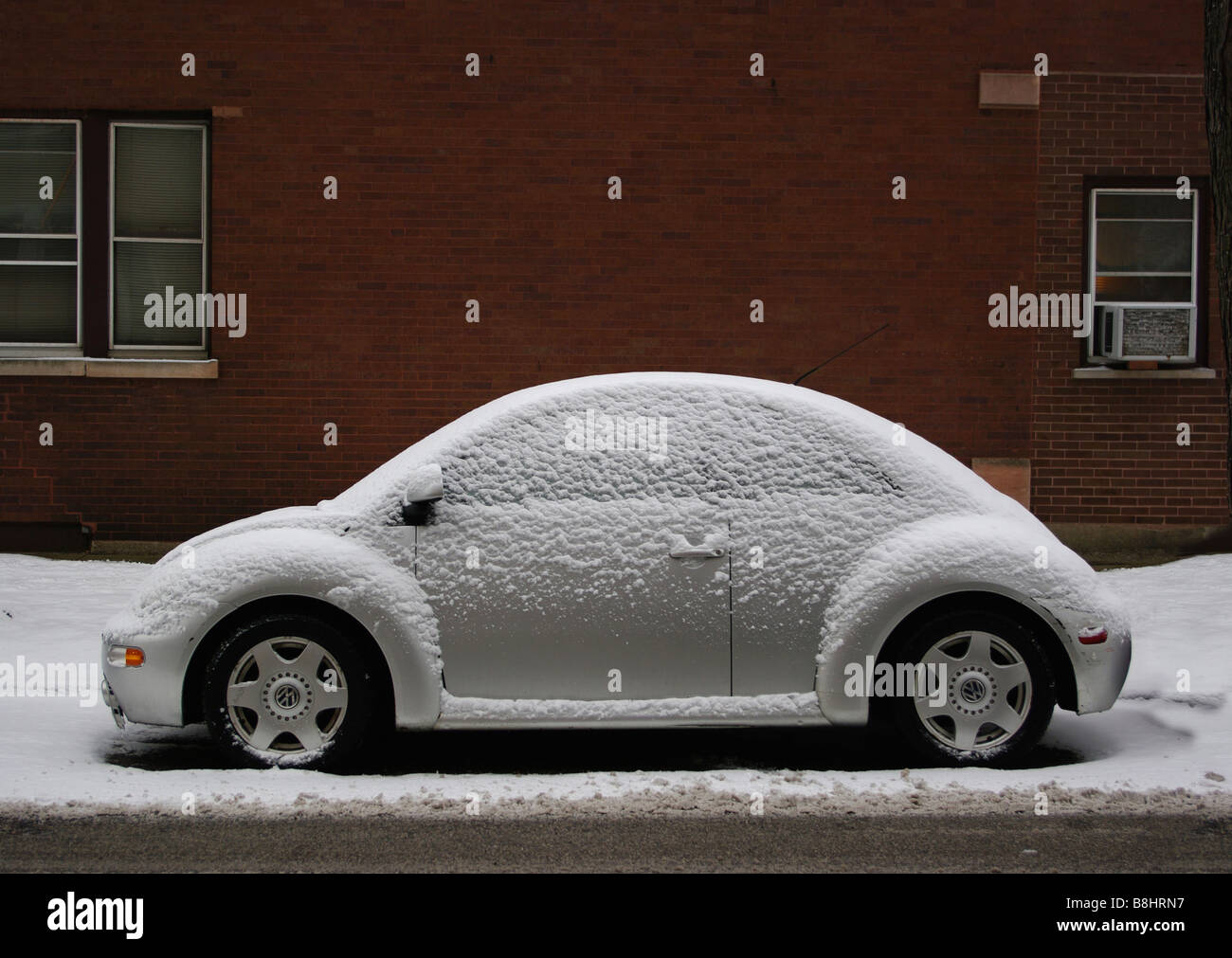 After a light snowfall, a Volkswagon Beetle sits frozen on a city ...