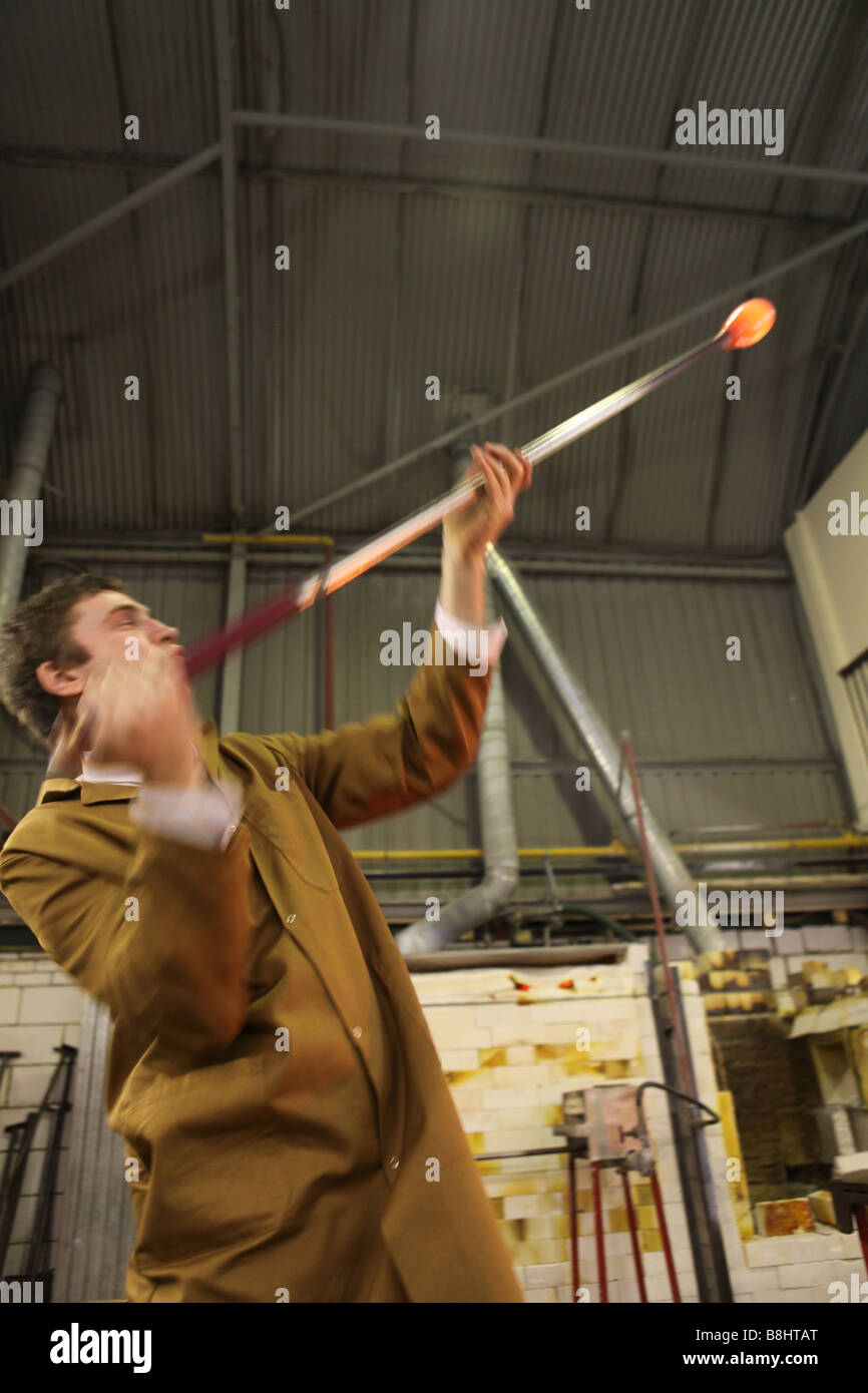a professional glass blower takes some molten glass out of a furnace ...