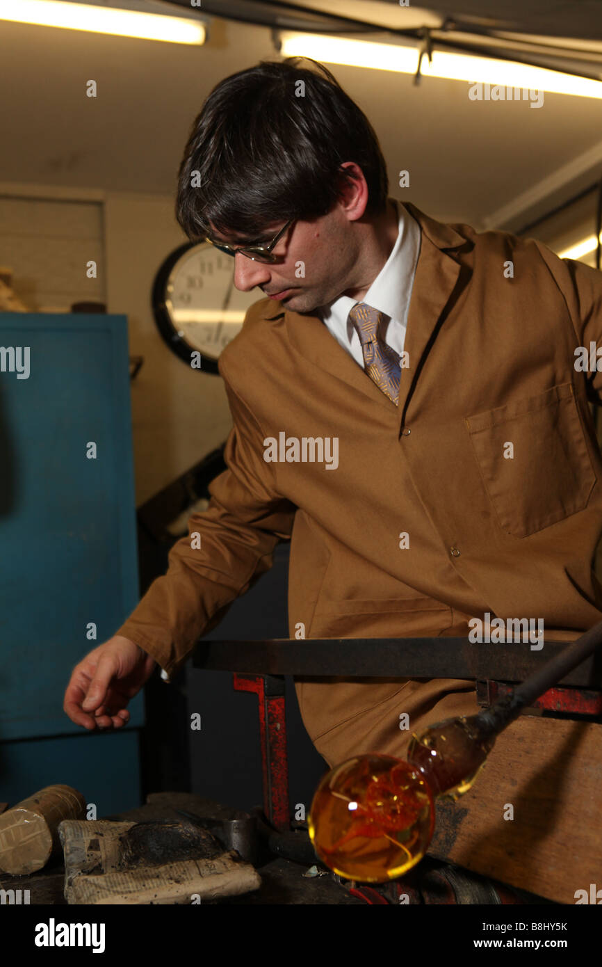 a professional glass blower takes some molten glass out of a furnace ...