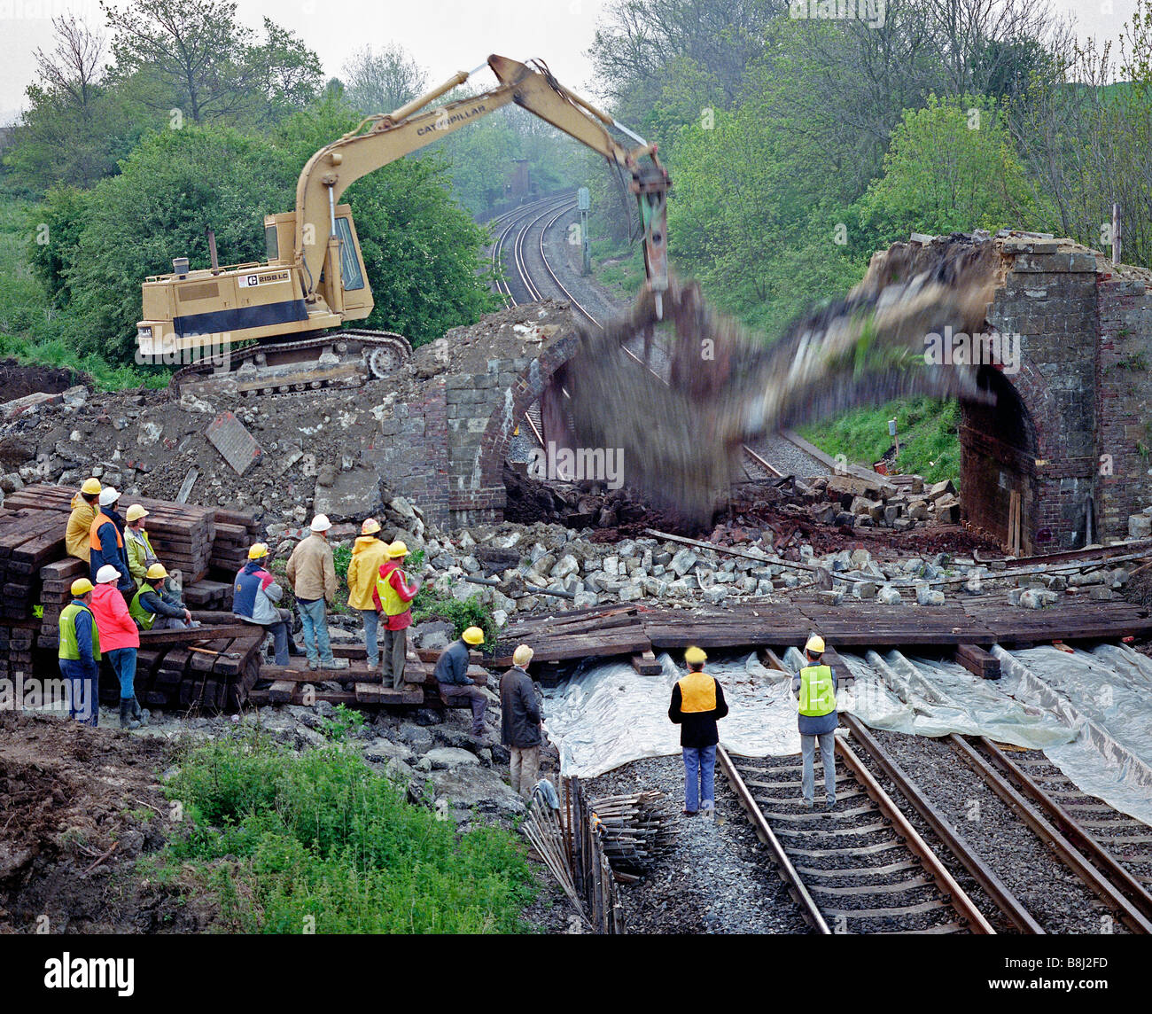 Hydraulic breaker demolishing narrow road bridge over a twin track ...