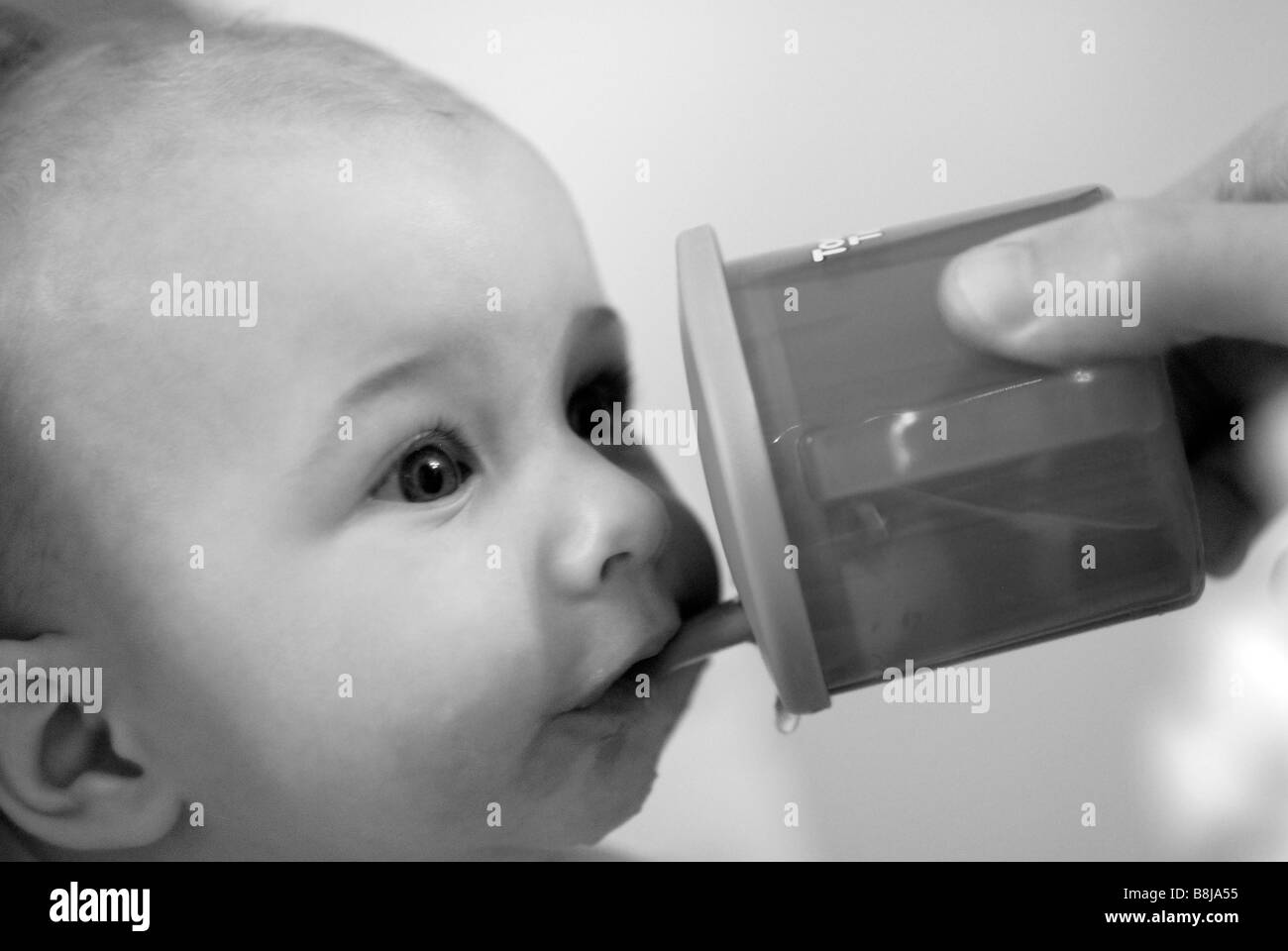 A baby boy drinks water from a baby beaker held by his father Stock ...