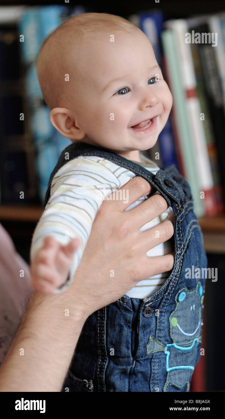 A baby boy smiles while standing and being supported by his father's ...