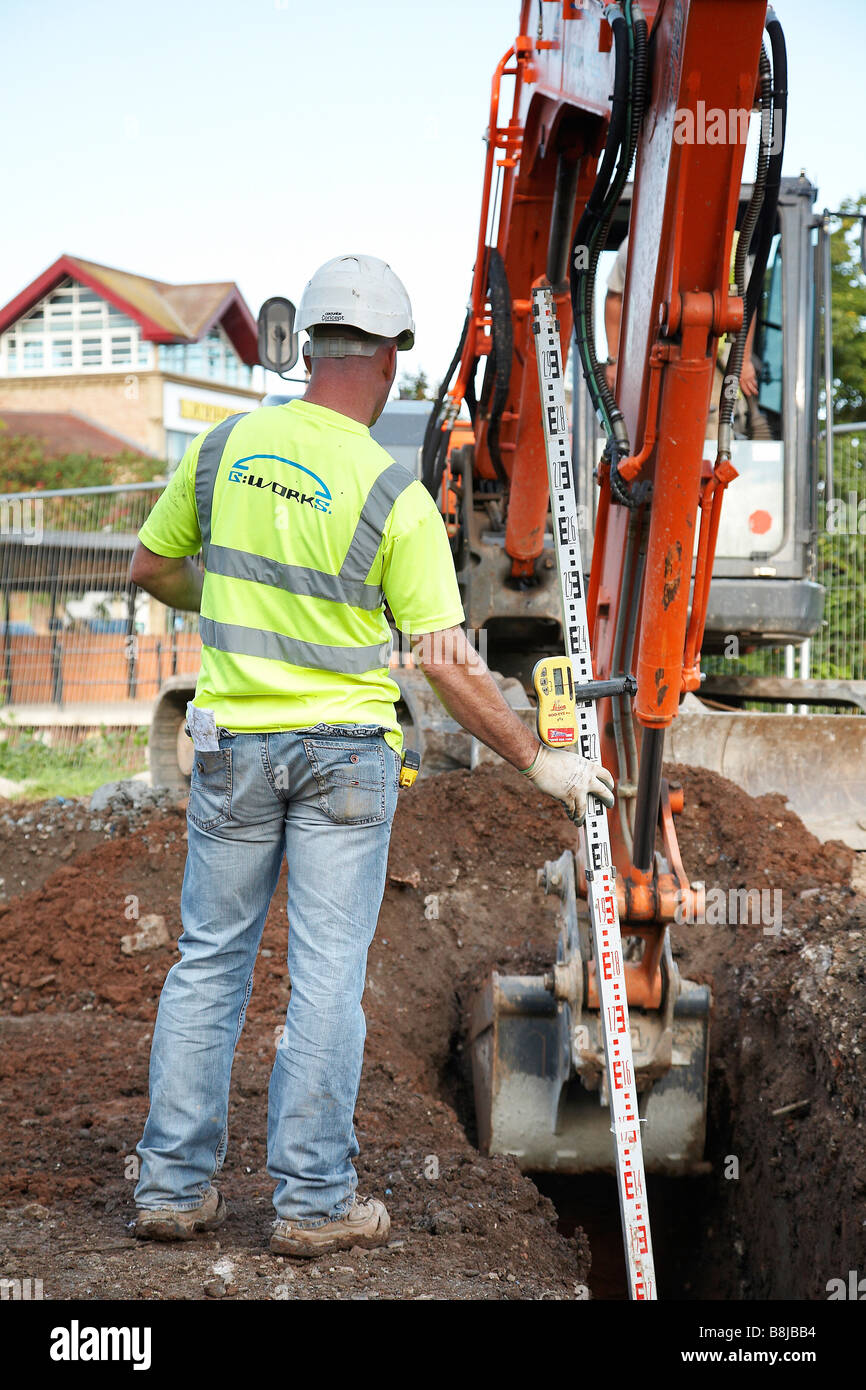 workman measures the depth of a trench dug by a jcb Stock Photo - Alamy