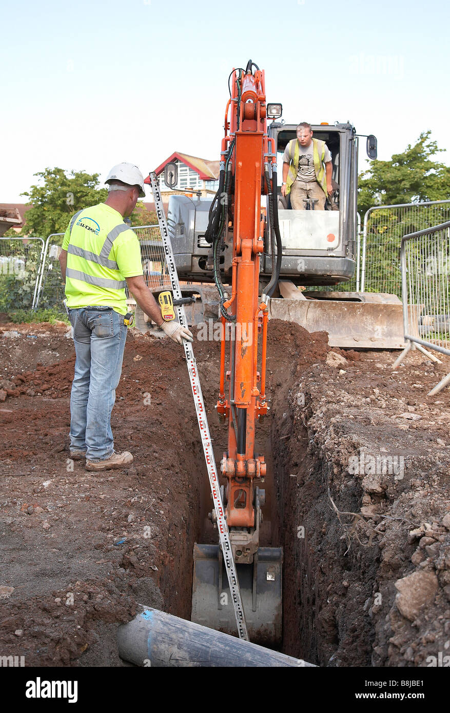 workman measures the depth of a trench dug by a jcb Stock Photo - Alamy