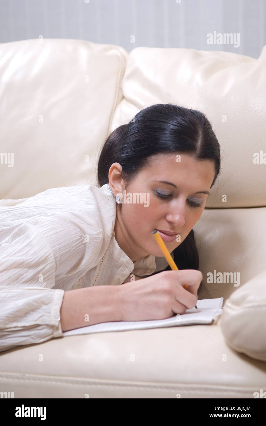 Beautiful young woman lying on sofa writing a letter Stock Photo - Alamy