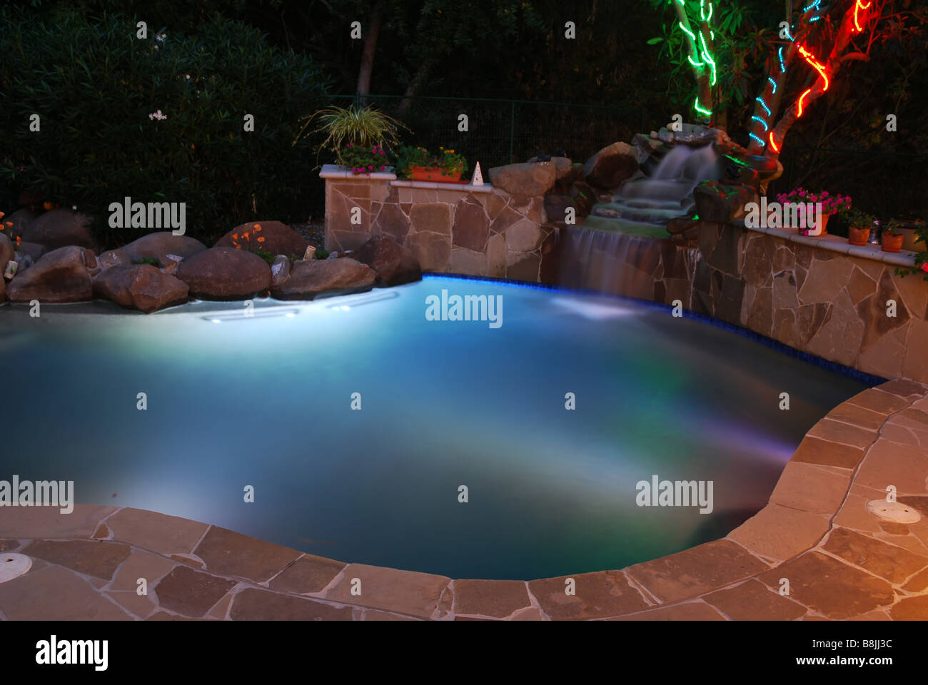 Custom swimming pool with waterfall illuminated at night Stock Photo ...