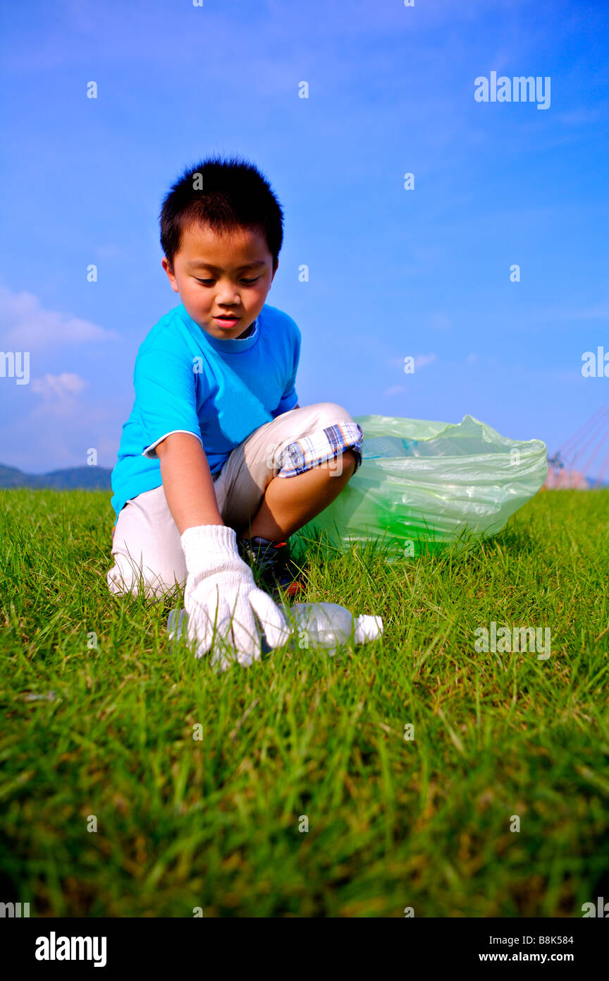 Little boy picking the empty bottle up and putting it into the garbage ...