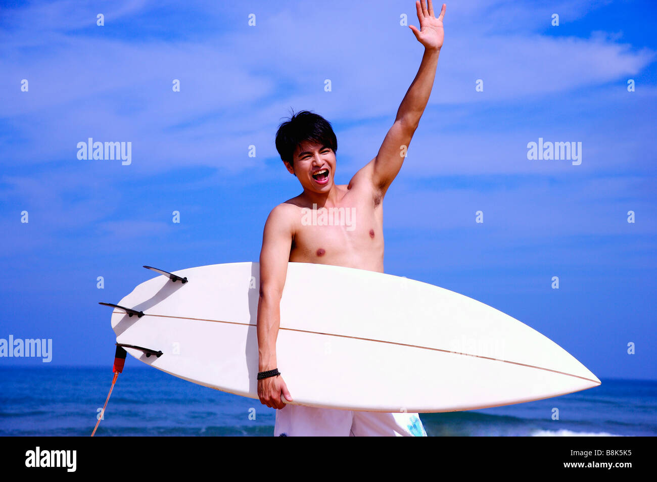 Man holding the surfboard waving one hand and smiling happily Stock ...