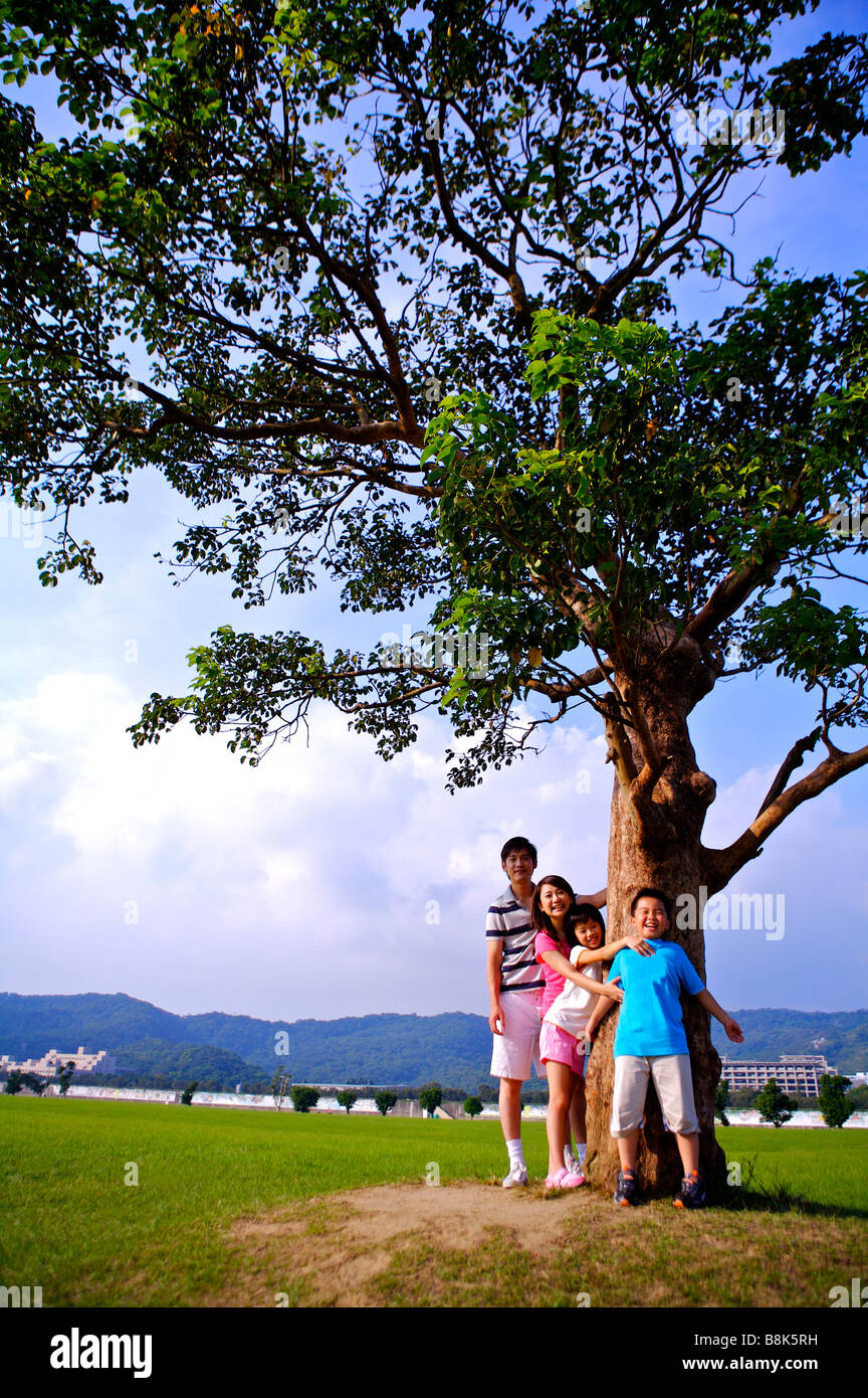 Young family with two children playing under a tall tree looking at the ...