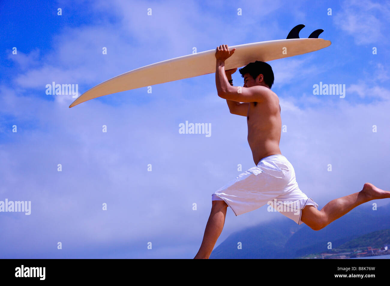 Young man carrying surfboard on head and jumping side view Stock Photo ...