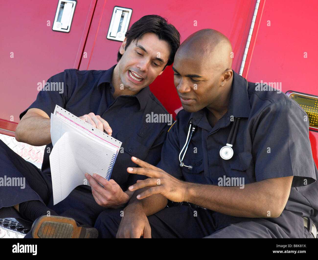 Two paramedics cheerfully doing paperwork, sitting by their ambulance ...