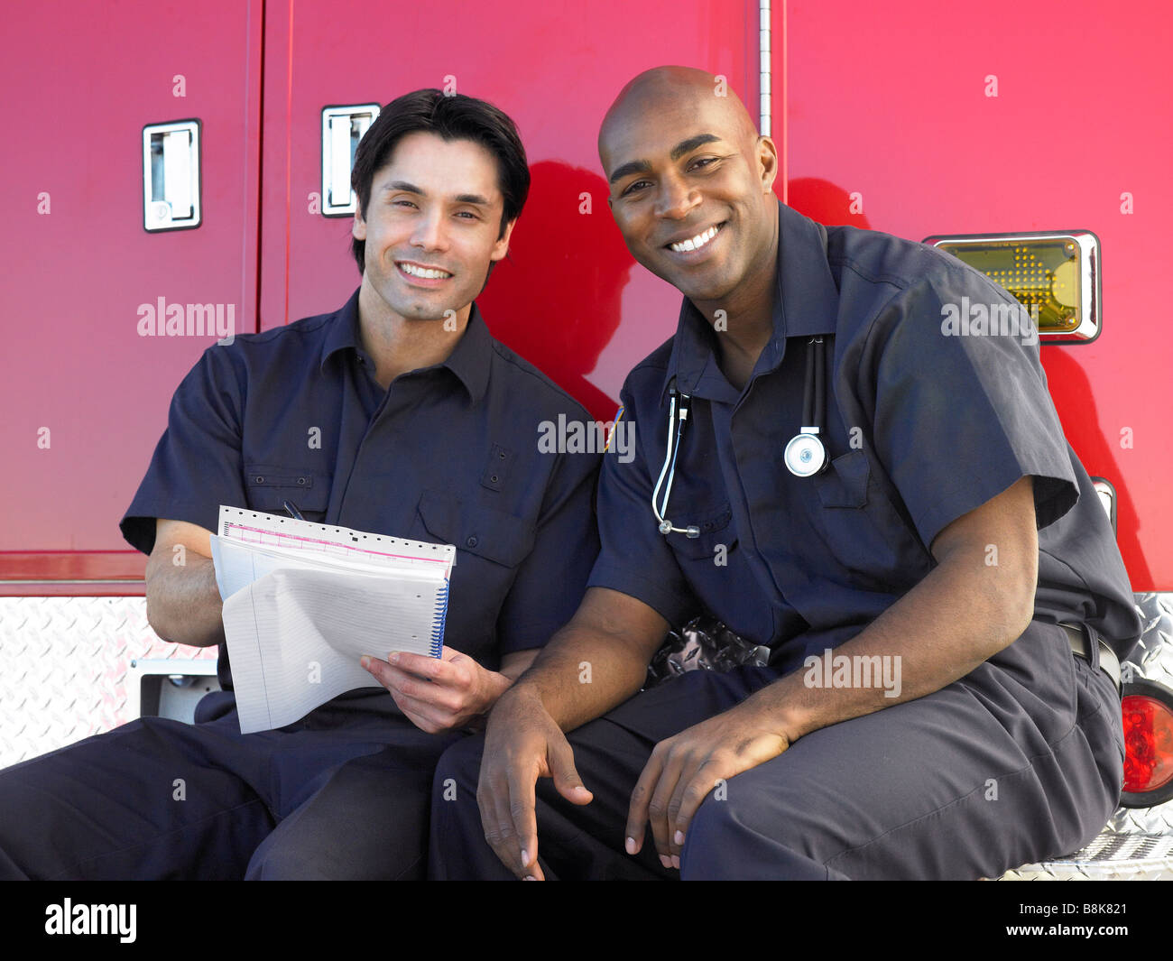 Two paramedics cheerfully doing paperwork, sitting by their ambulance ...