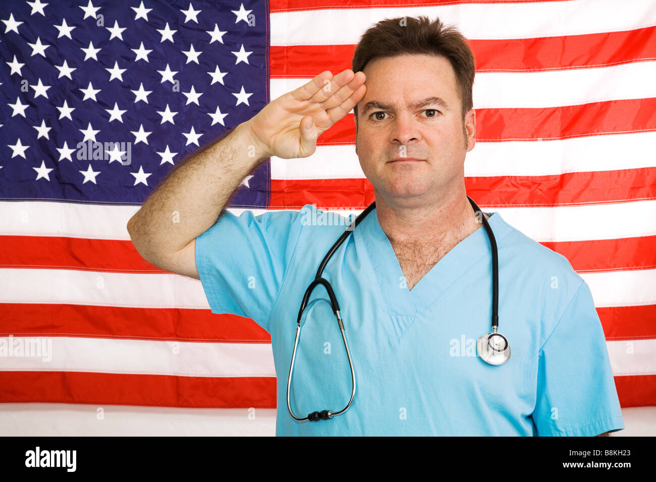 Doctor in scrubs with stethoscope saluting the American Flag ...