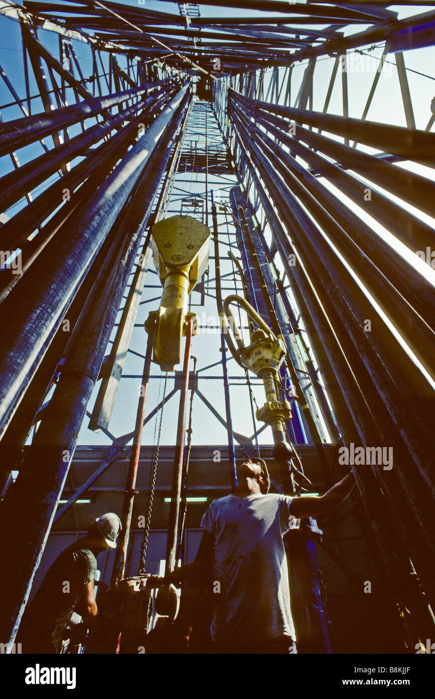 Two workers with drill bit, drill collar and piping on offshore oil rig ...