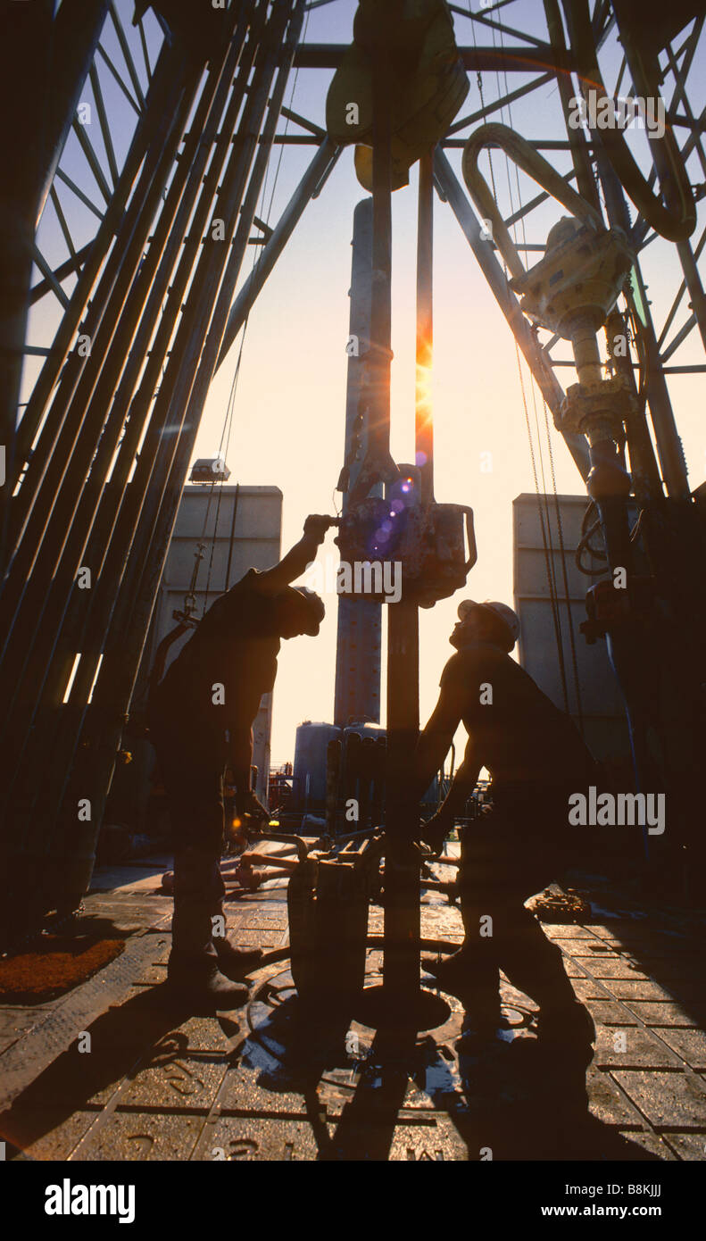 Two workers with drill bit, drill collar and piping on offshore oil rig ...