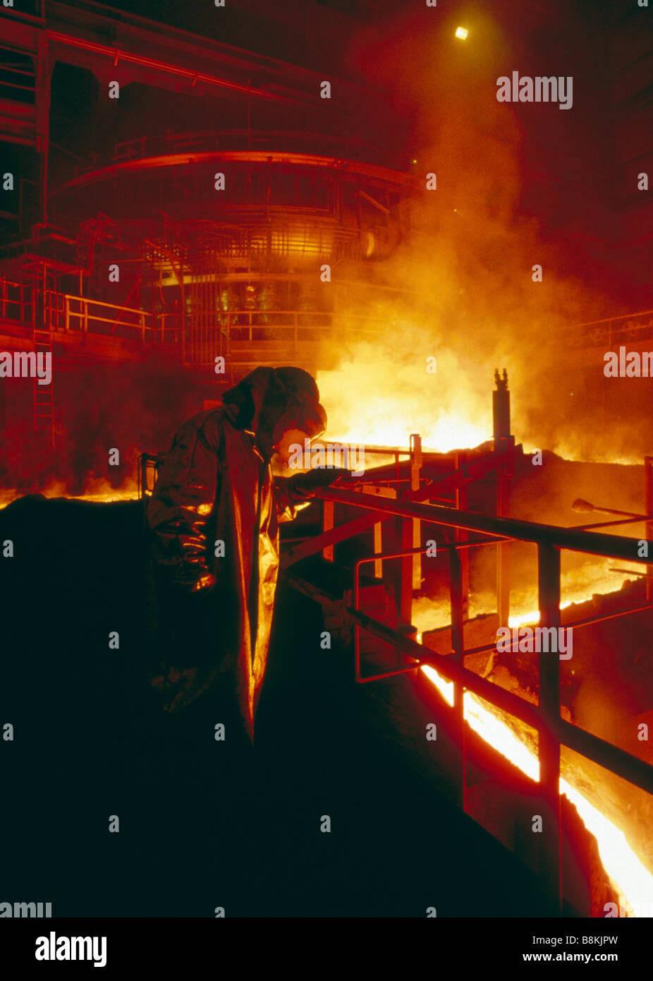 Steelworker in protective suit watches molten steel pour from just ...