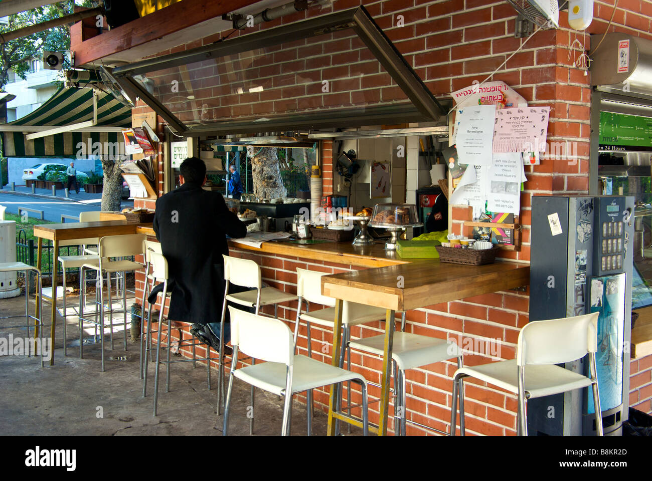 Customer reading newspaper on coffee break seated on stool at a cafe ...