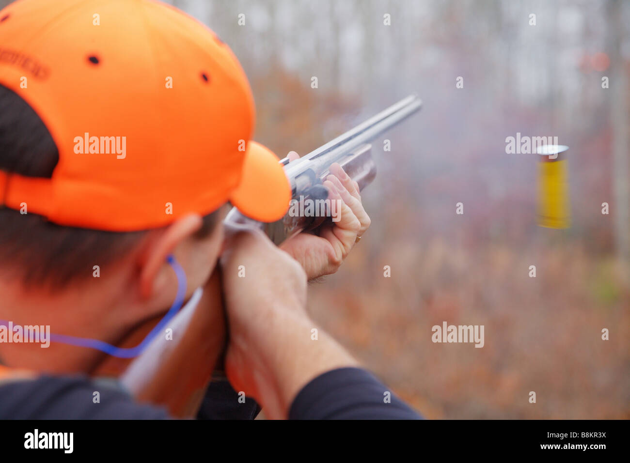 OVER THE SHOULDER VIEW OF SPORTING CLAY SHOOTER IN ORANGE HAT FIRING AT ...