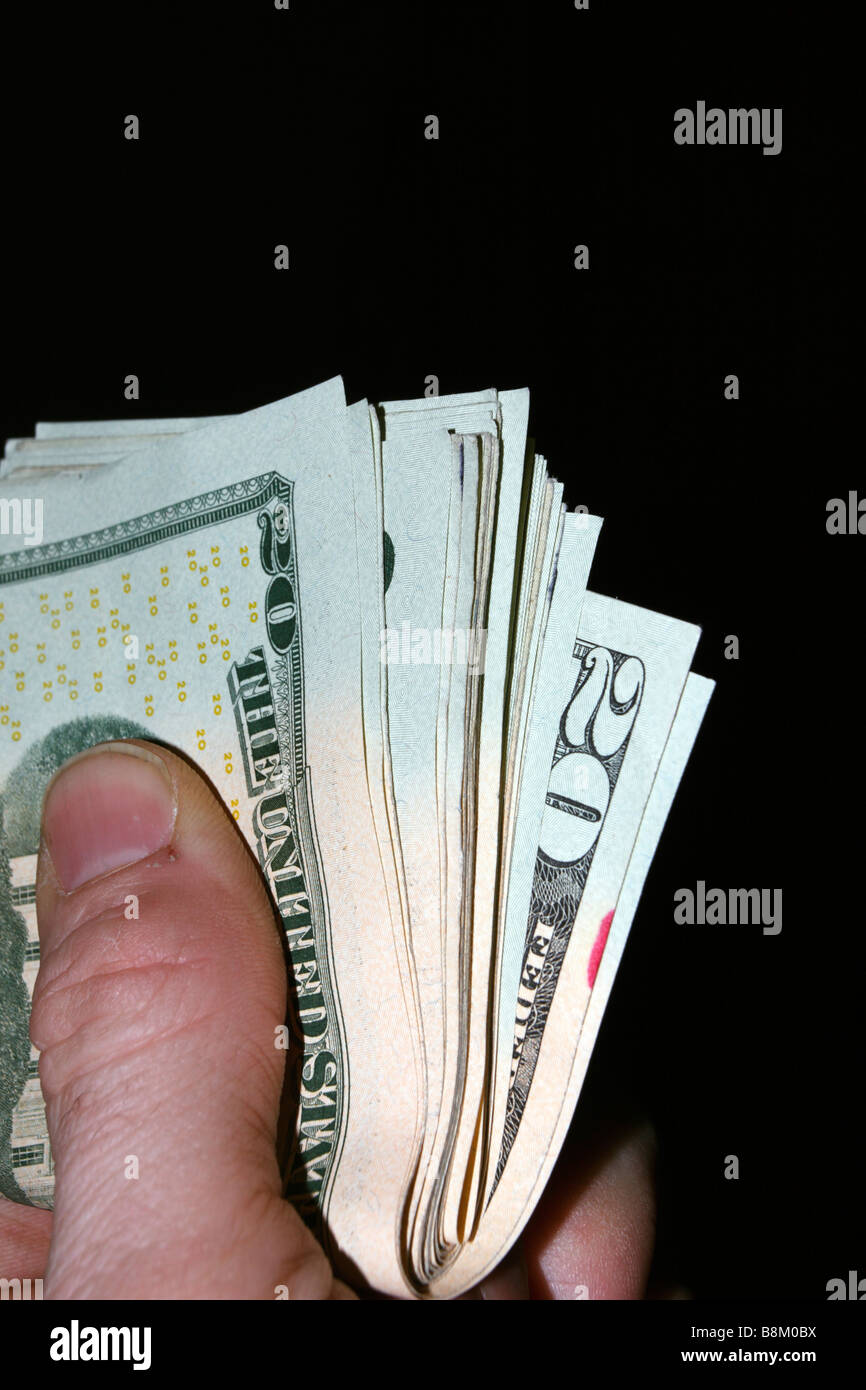 Thumb of left hand holding folded USA twenty dollar bills. On black ...