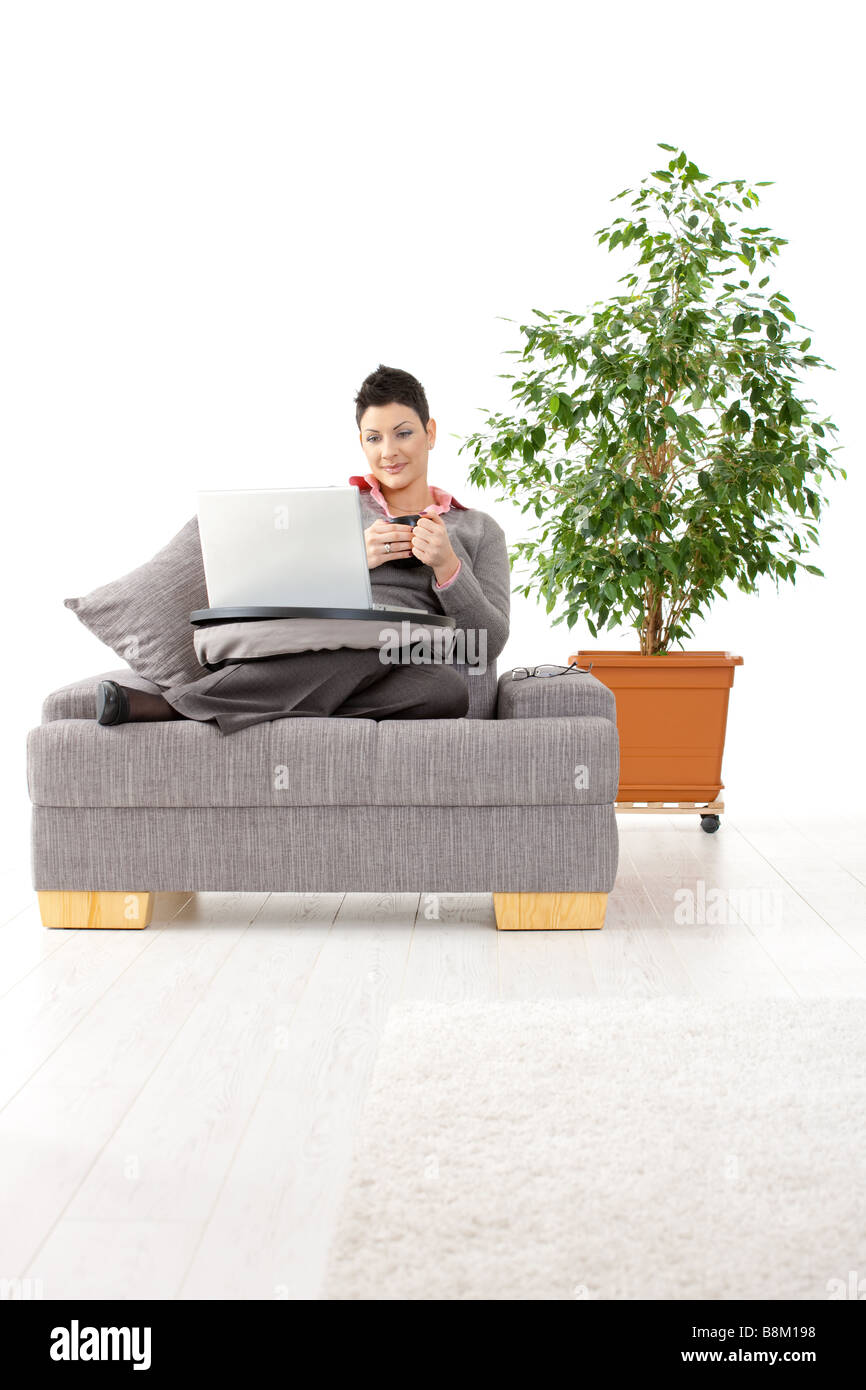 Young woman sitting on couch teleworking on laptop computer at home ...