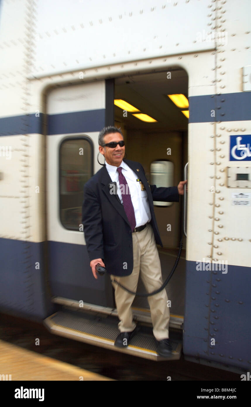 A smiling conductor leaning out of a train that is leaving the ...