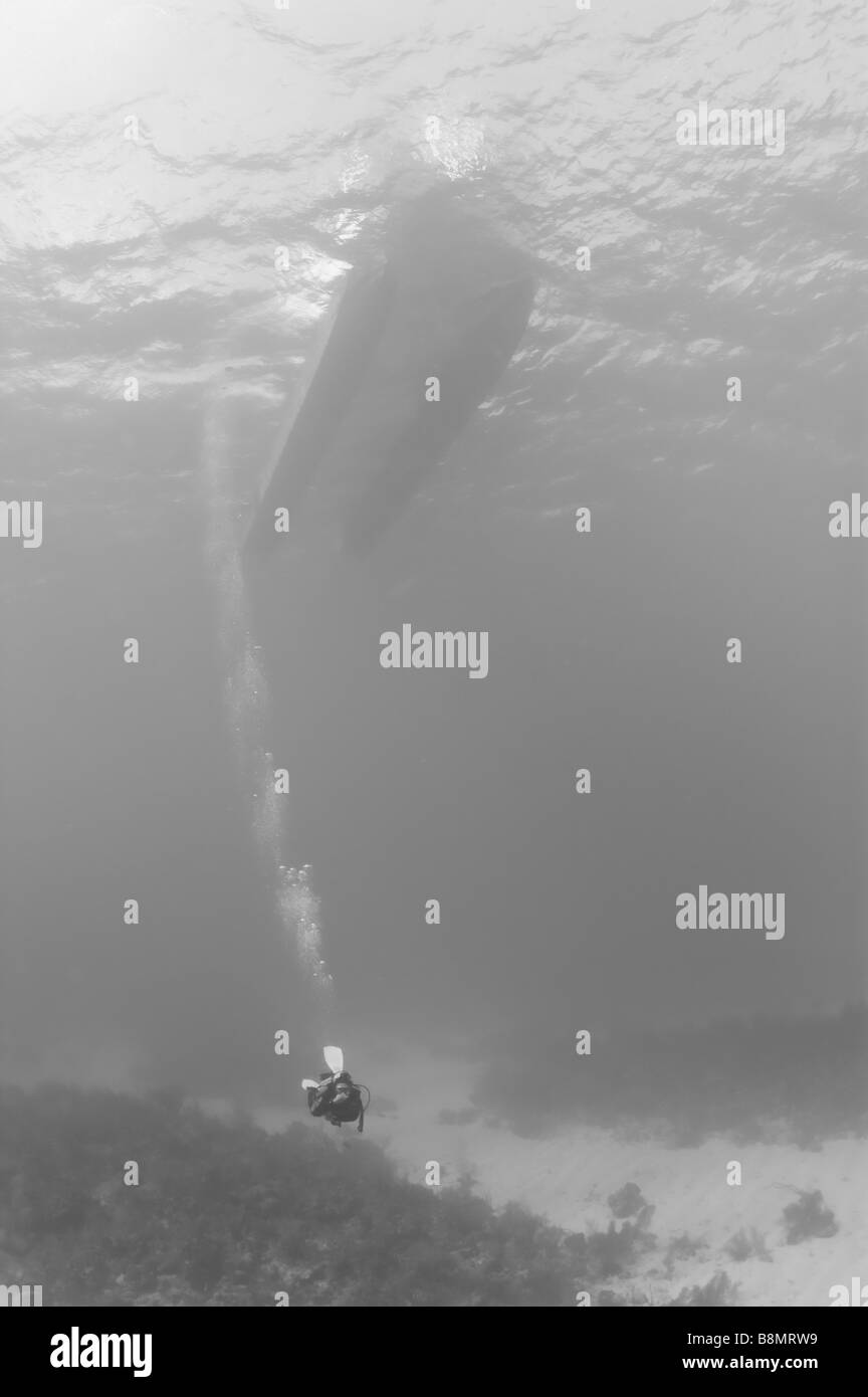Scuber diver diving deep below a boat floating on the surface of the ...