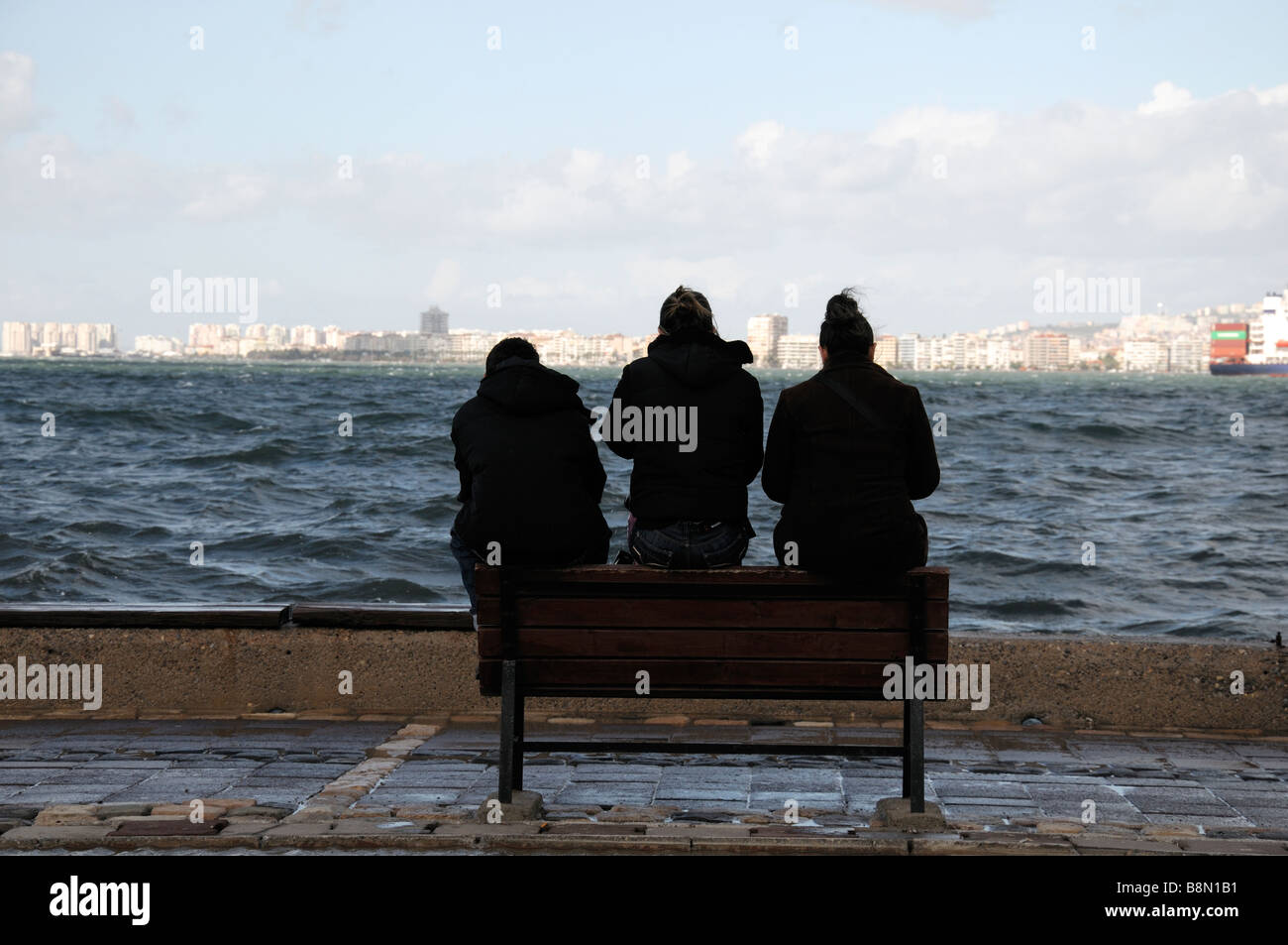 Three people friends sit sitting together on a Bench face look looking ...