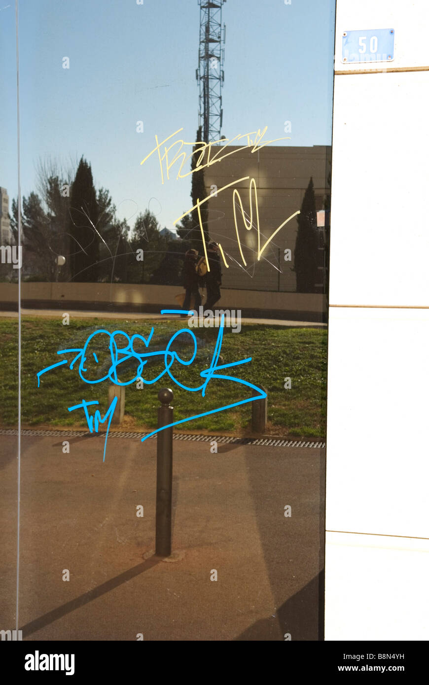 a mirror window covered with tags and graffiti reflects people walking ...