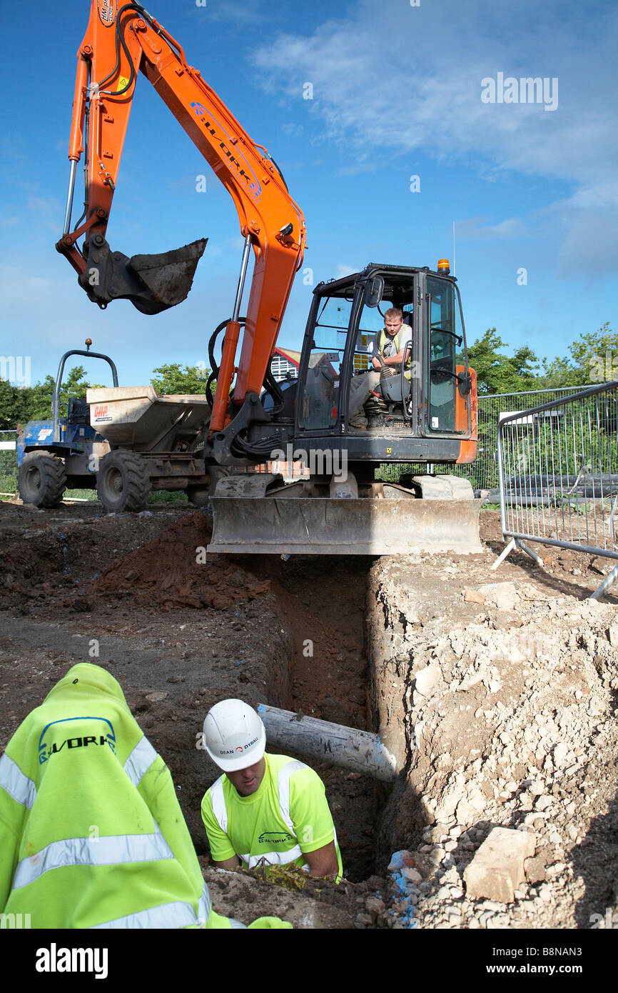 Jcb digging a trench on a construction site while a workman digs around ...