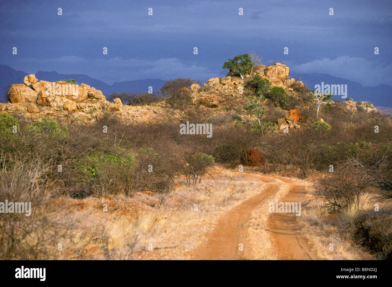 Dirt track leading around a granite outcrop against a backdrop of dark ...