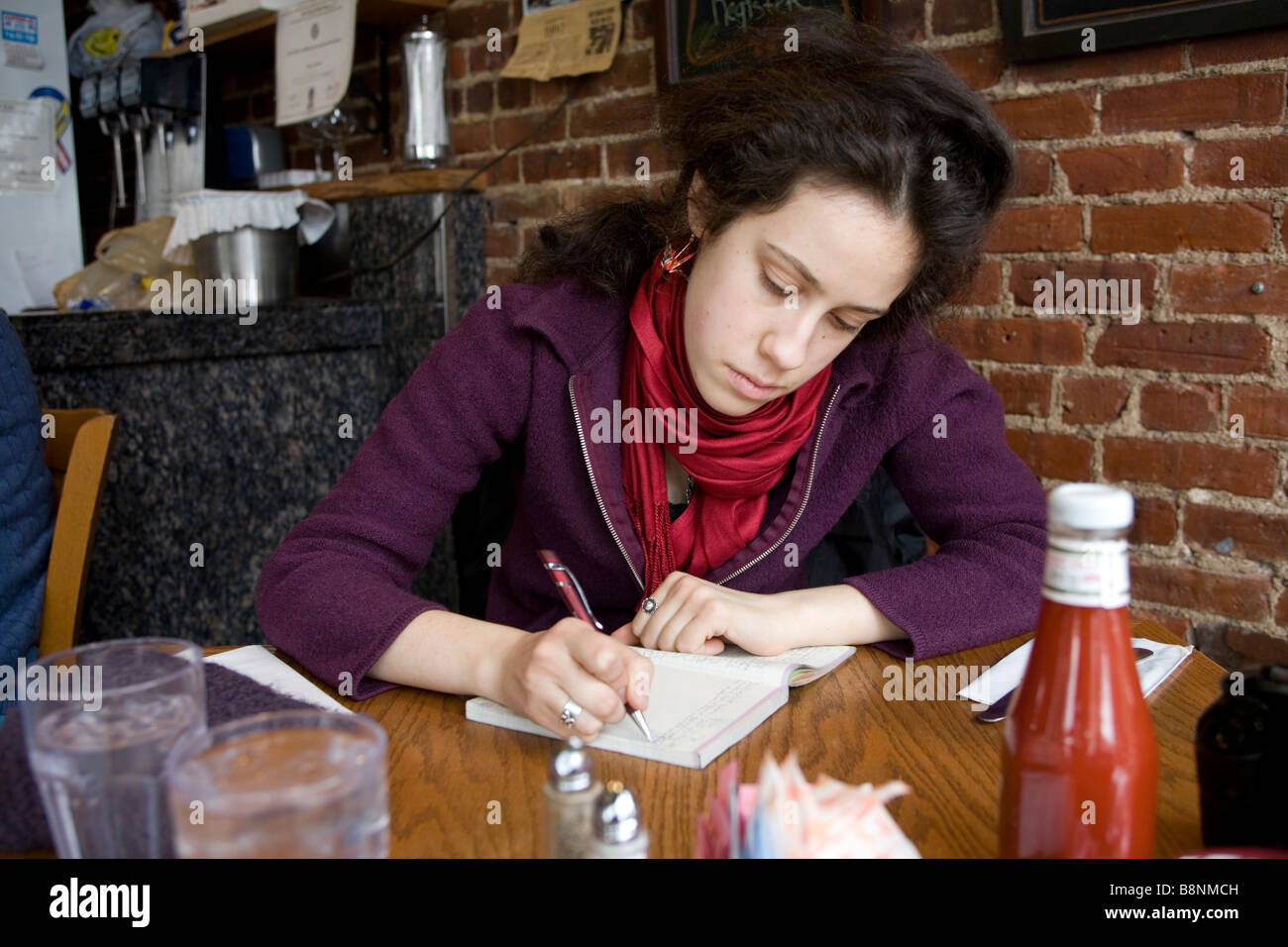 College student intently writing in her journal at a cafe in Brooklyn ...