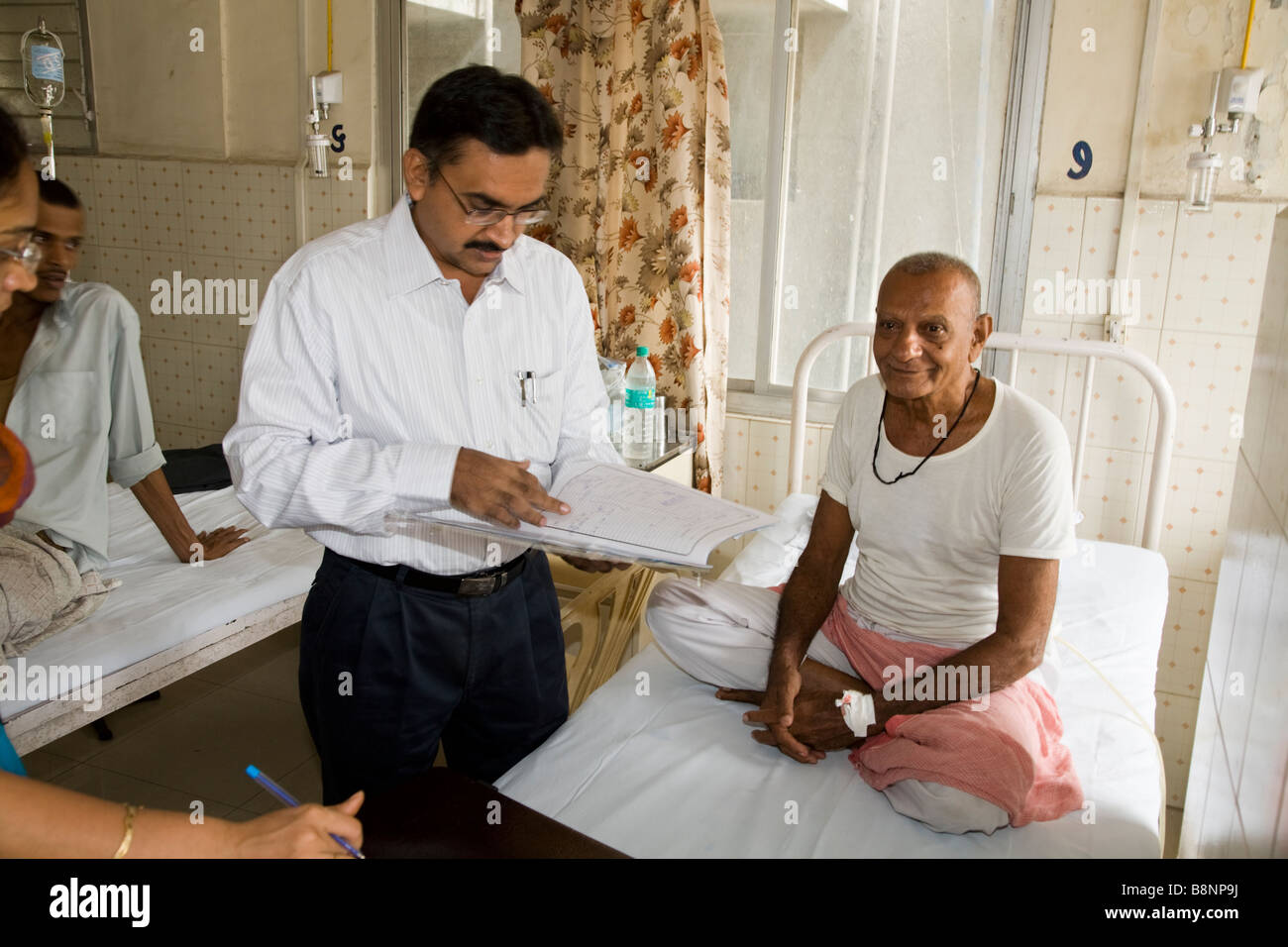 Indian doctor, with notes, talking to a patient. General ward of the ...