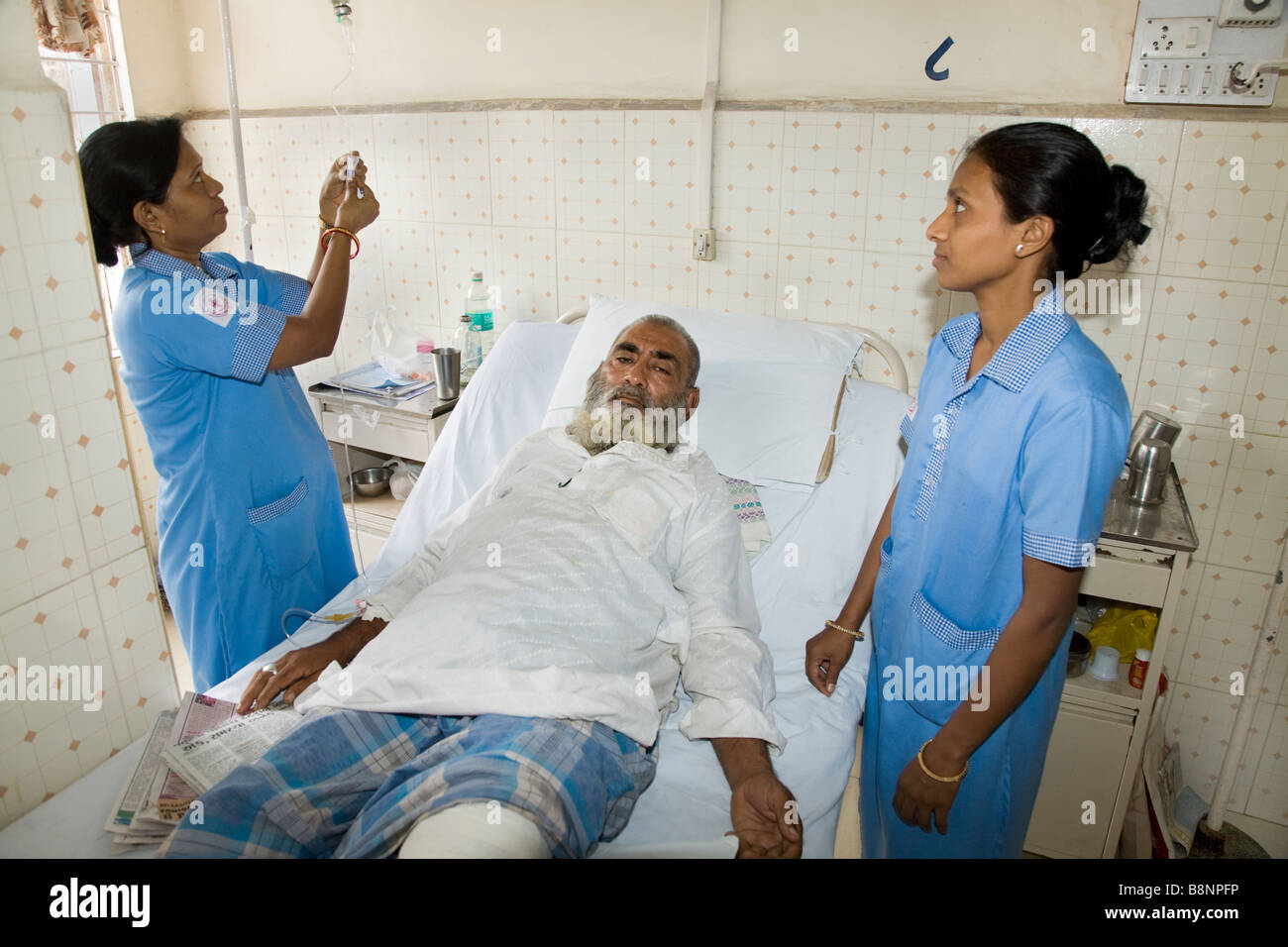Nurses set up an intraveinous drip to a patient on a general ward of ...