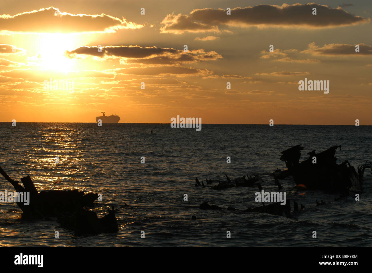 A cruiseship sails off into the sunset, with a piece of ship wreckage ...