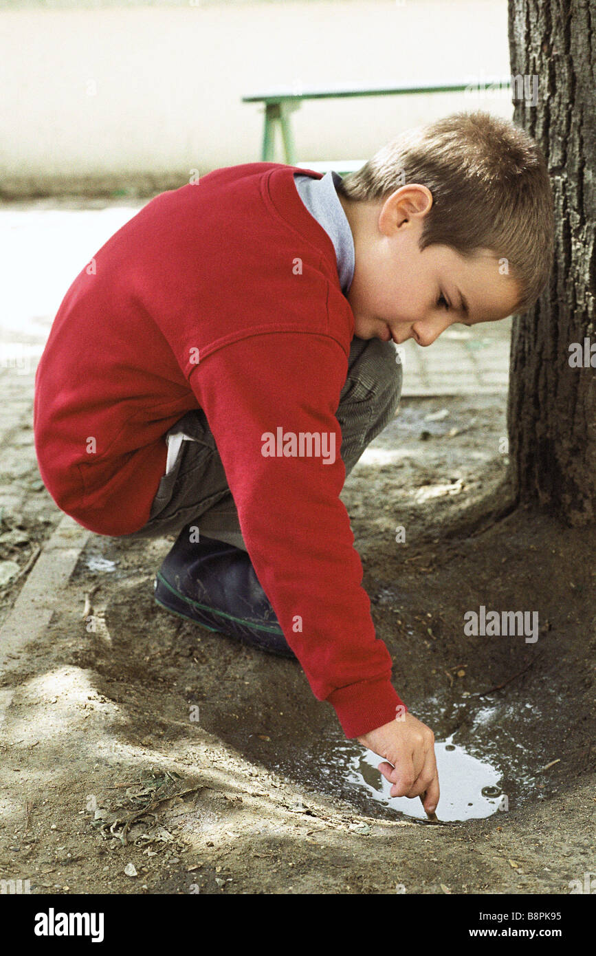 Boy crouching, playing in puddle, side view Stock Photo - Alamy