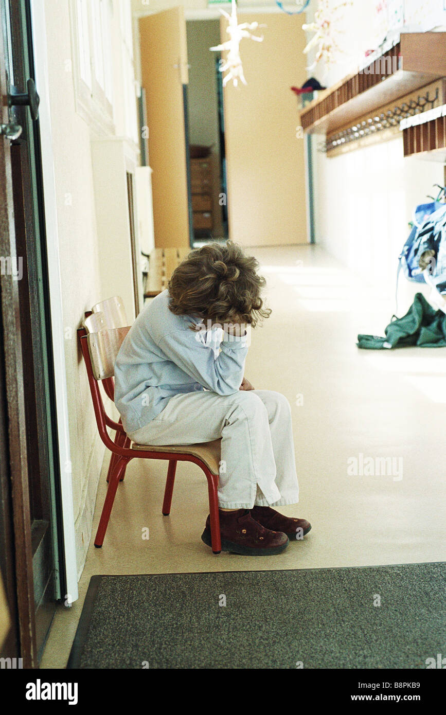 Child sitting alone in corridor, holding head Stock Photo - Alamy