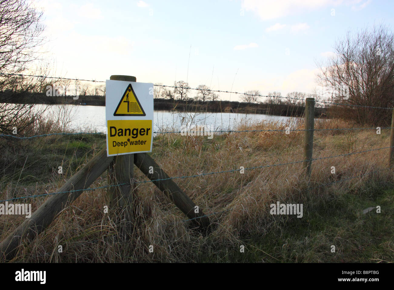 danger deep water sign attached to a fence at the side of a flooded ...