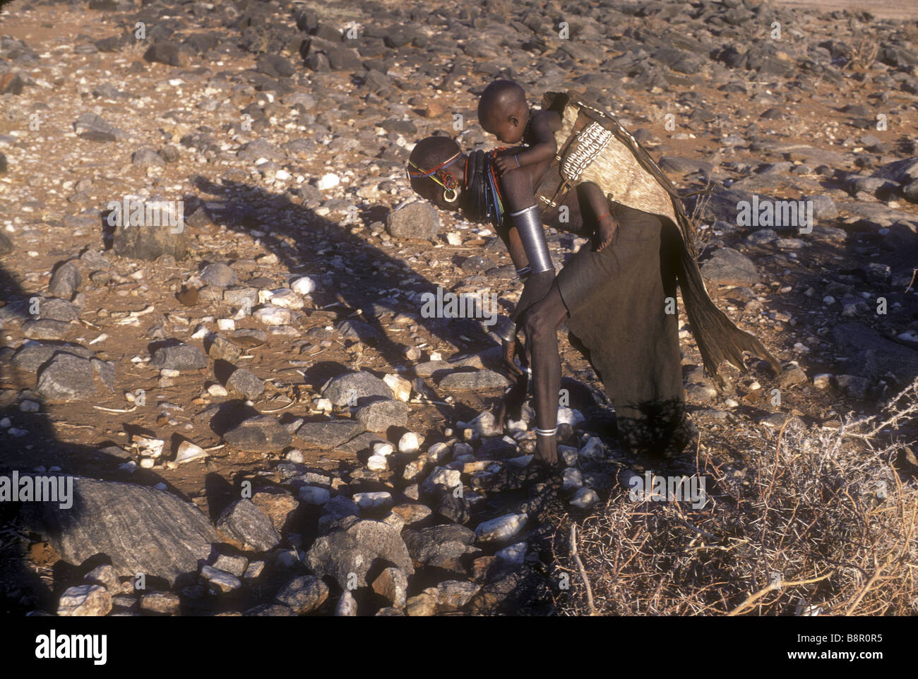 Rendille grandmother gathering stones to put in a line outside her hut ...