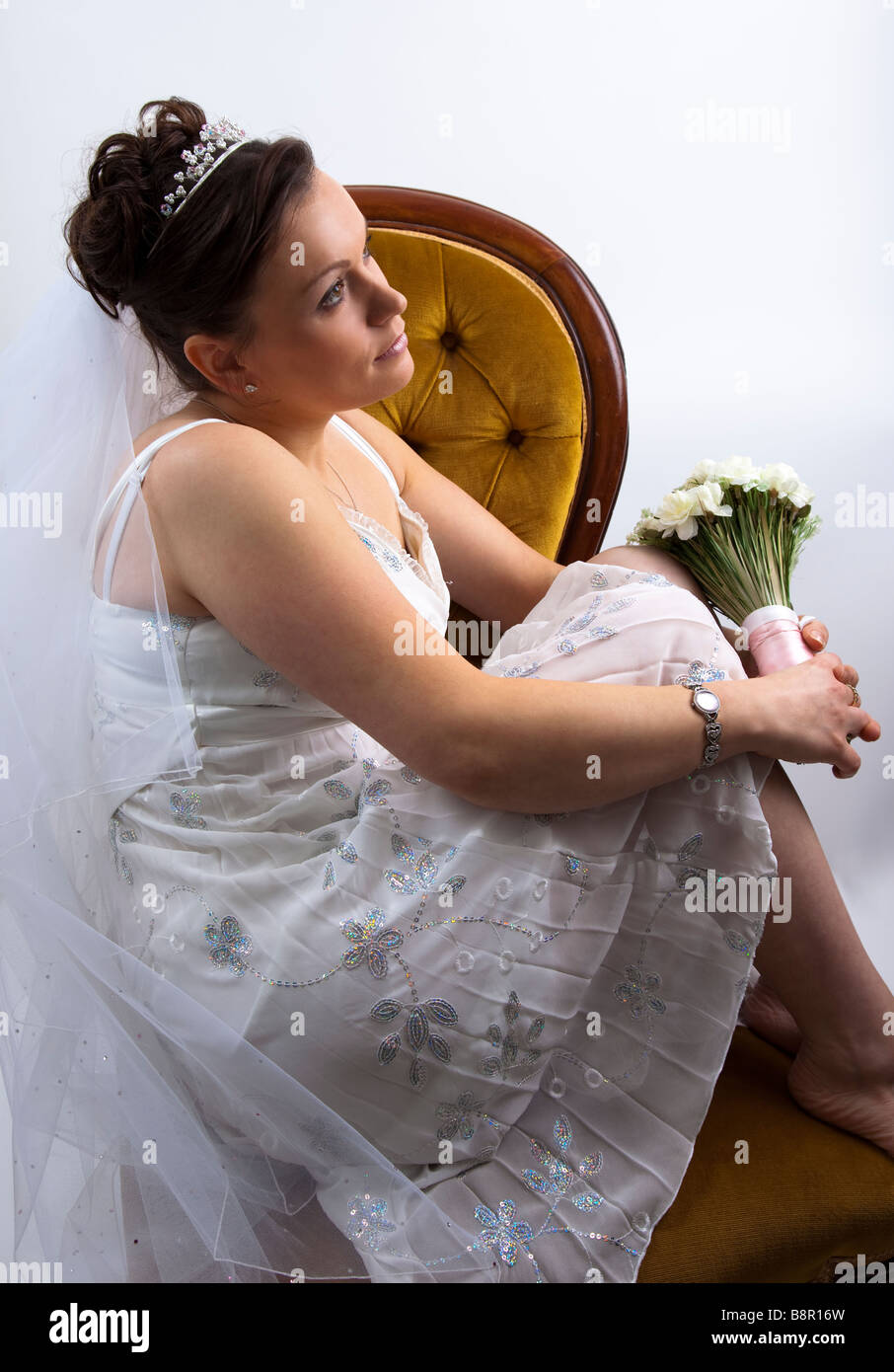 Bride in white posing on antique chair holding bouquet and bare footed ...