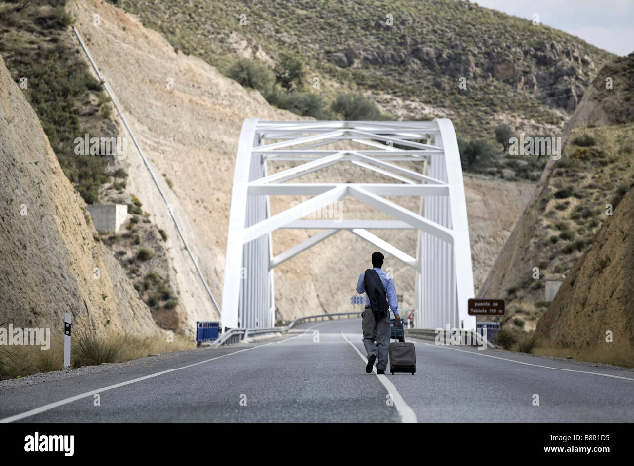 Man dresses in suit walks along a road towards a bridge Stock Photo - Alamy