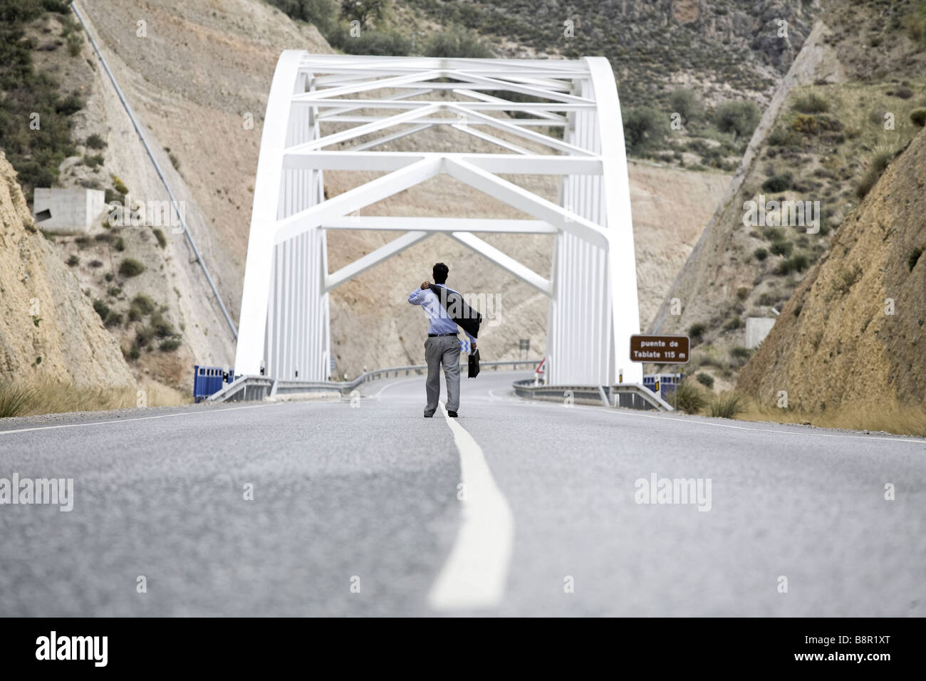 Man dresses in suit walks along a road towards a bridge Stock Photo - Alamy