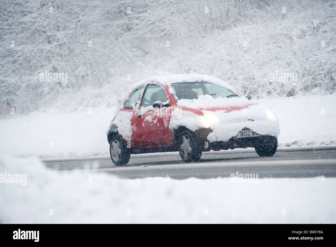 Red car driving slowly on a snowy road in winter in England with ...