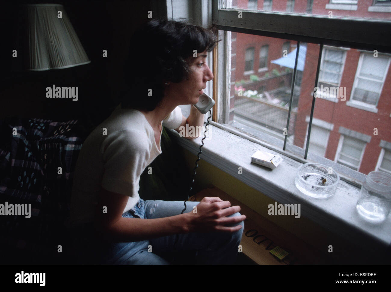 Woman, thirties, looks out the open window onto a city street as she ...